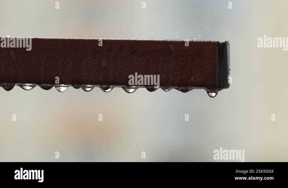 Rain water droplets falling or dripping from the metal railing - close ...