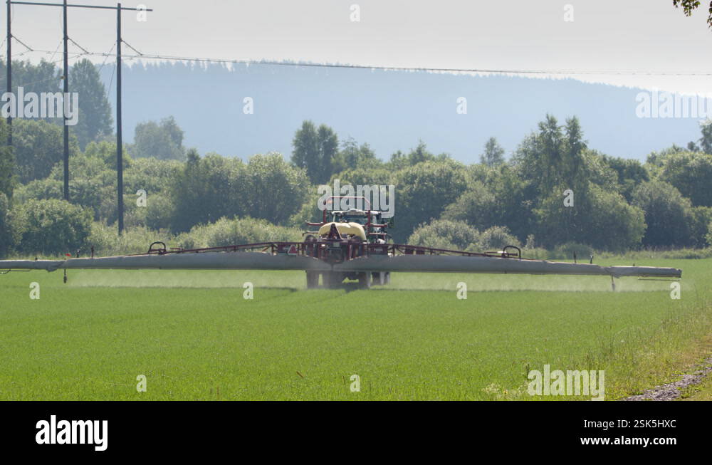 Pesticide crop spraying on farm land with sprayer tractor, long shot ...