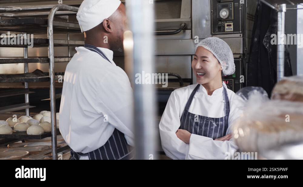 Happy diverse bakers in bakery kitchen with arms crossed talking in ...