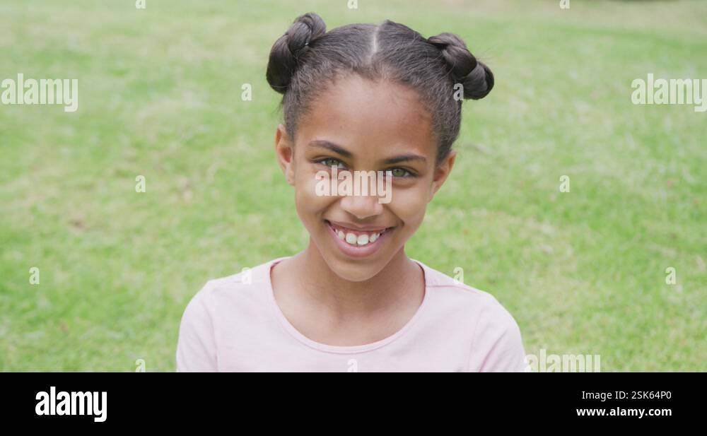 Video portrait of smiling biracial schoolgirl in school playing field ...