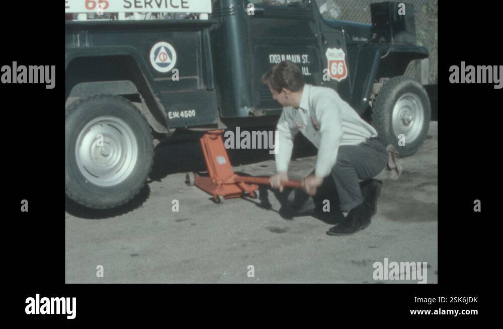 1960s: kneeling gas station mechanic with rag in back pocket raises ...