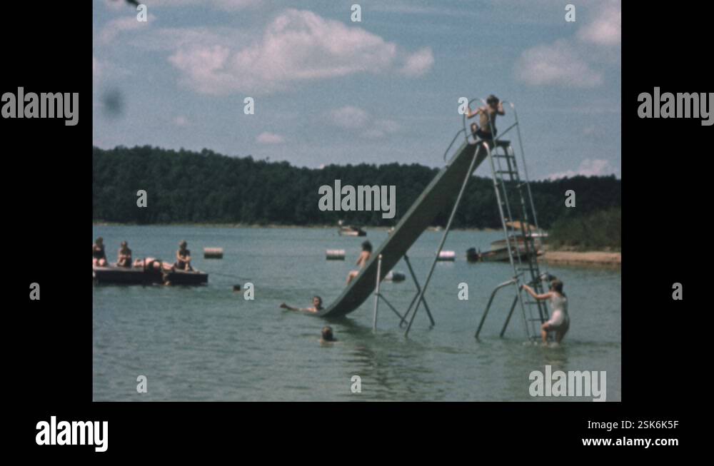 1960s: people relax on wooden dock in lake, kids climb slide, slide ...