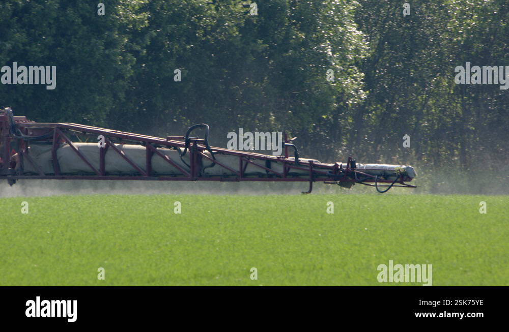 Crops on farm land being sprayed by boom arm of sprayer tractor, tele ...