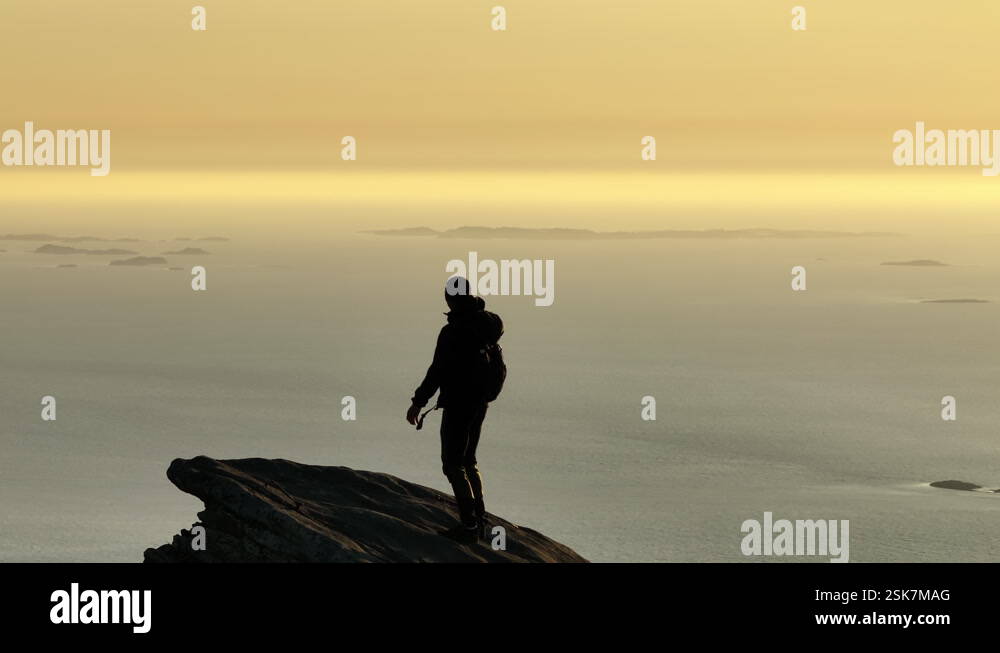 Climber silhouette on arctic mountain lift arms n midnight sun; drone ...