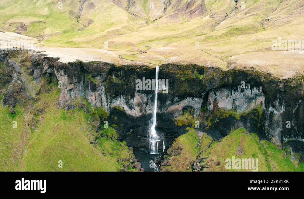 A long, thin waterfall on a high rocky escarpment in the mountains ...