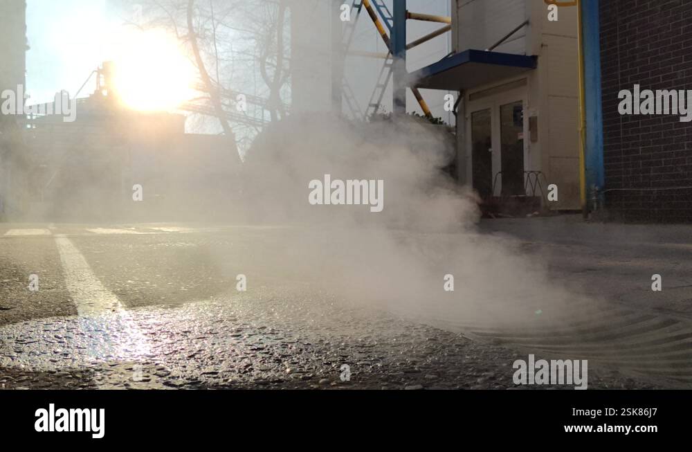 Smoke rises from a manhole cover in a street - closeup - sun blazes in ...