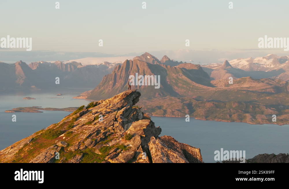 Hiker on Norway arctic island mountain cliff edge in midnight sun glow ...