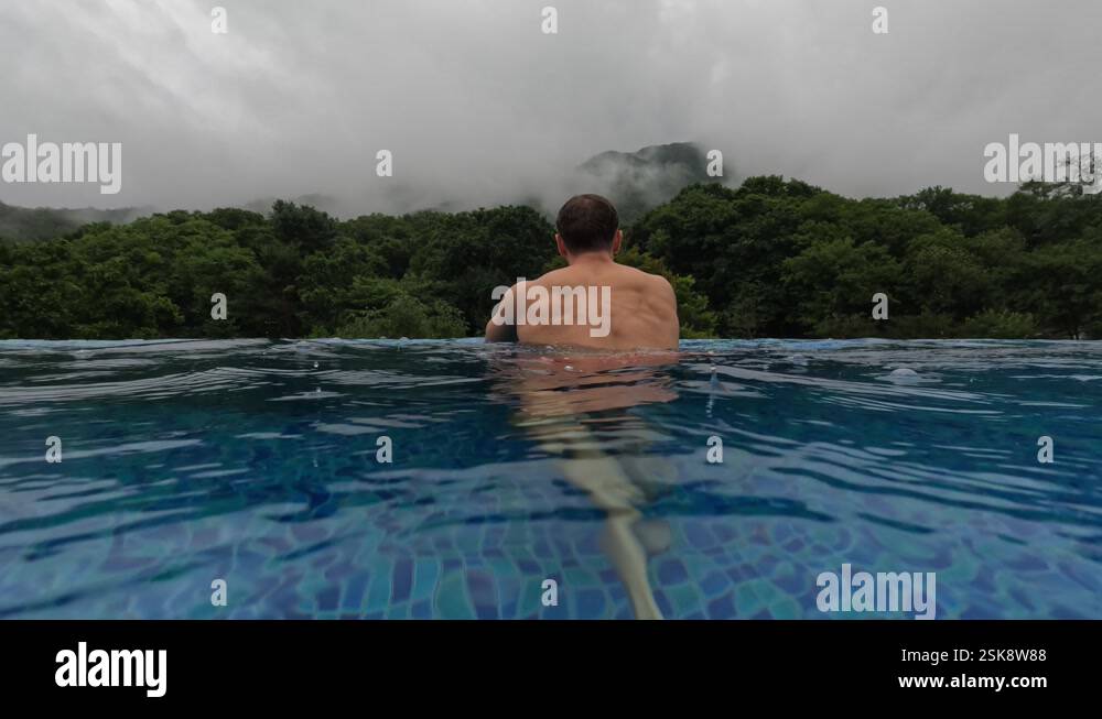 A Muscular Man Walks Inside Infinity Pool With Lush Mountain View on ...