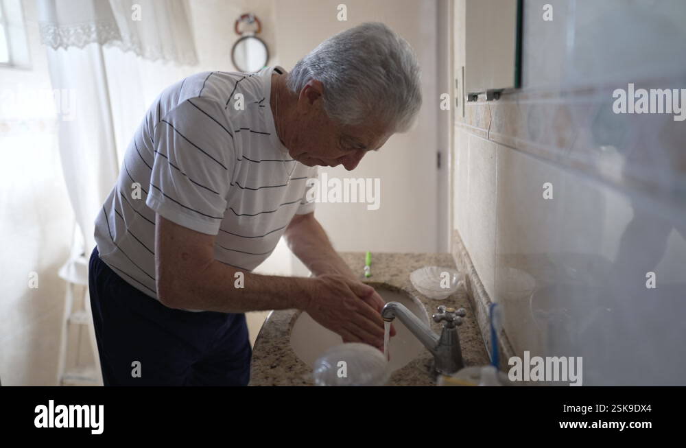 Senior man morning routine, washing face and brushing teeth in front of ...