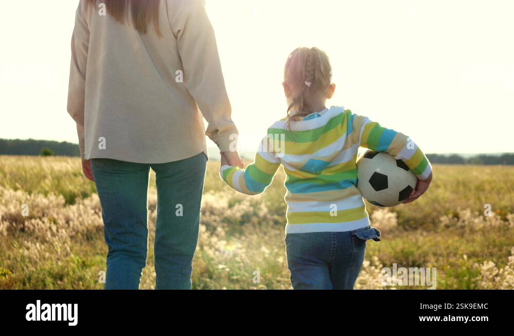 mother holding daughter hand go walk. girl walking along soccer ball ...