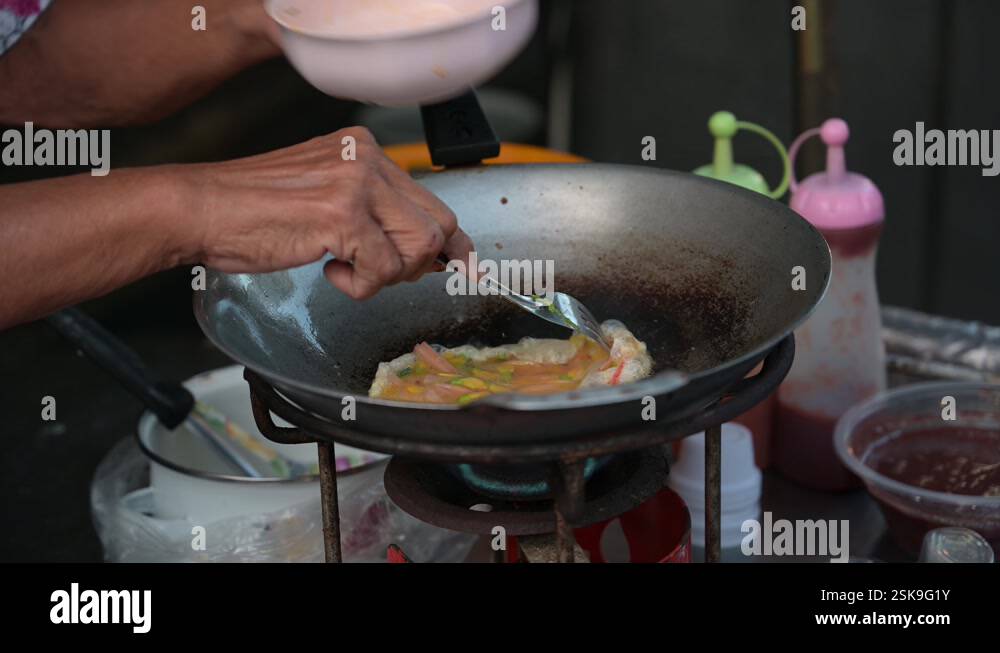 Street food vendor pouring scrambled eggs in a wok and adjusting the ...