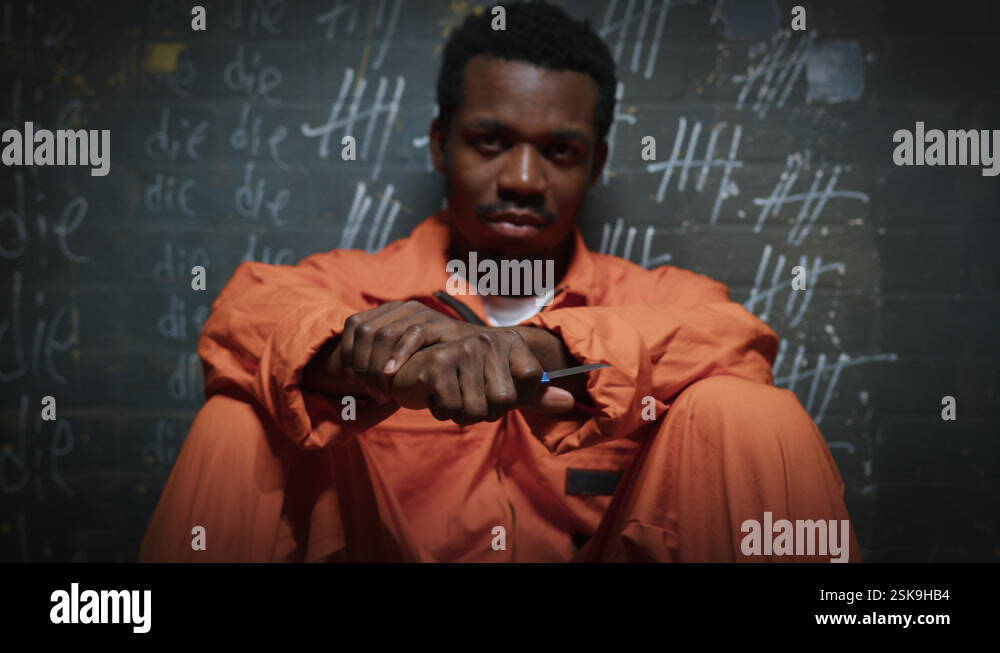 Black inmate sits on floor with back against wall with sharpening in ...