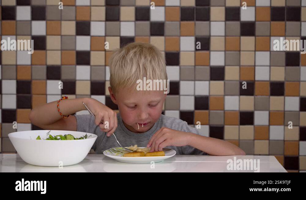 Blonde child boy at dining room table eats dish of nuggets and pasta ...