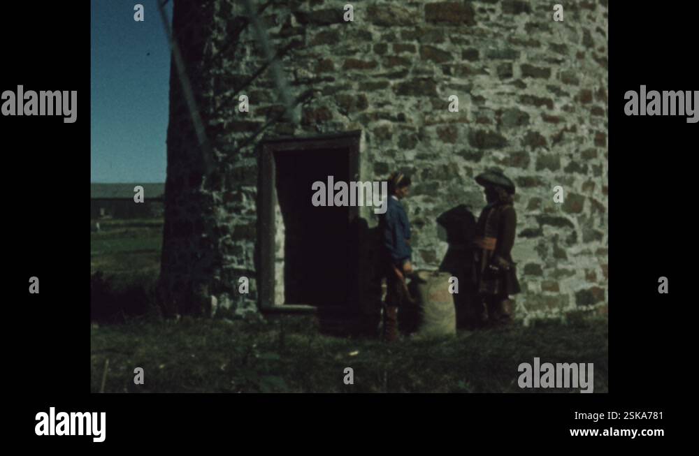 1960s: Two men stand outside windmill talking, one holds full sack over ...