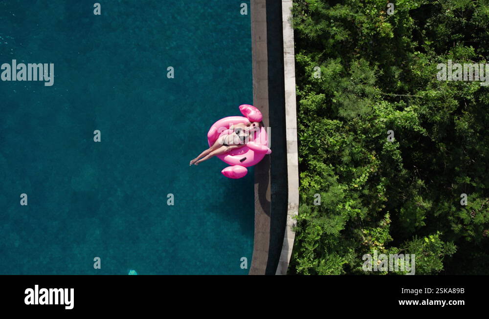 Woman chilling in infinity pool with pink inflatable flamingo ...