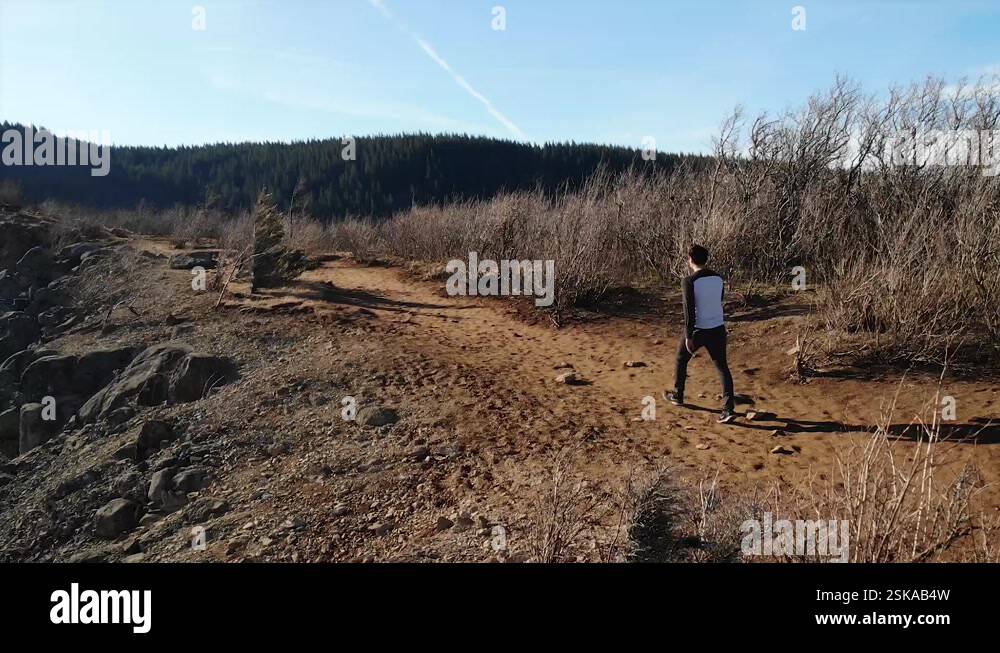 Drone follows a male model walking on a dirt trail. Boy walks next to a ...