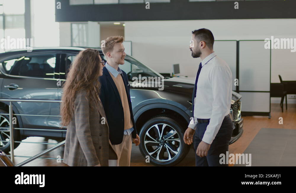 Male Sales Manager Welcoming Young Customers at Car Dealership Stock ...