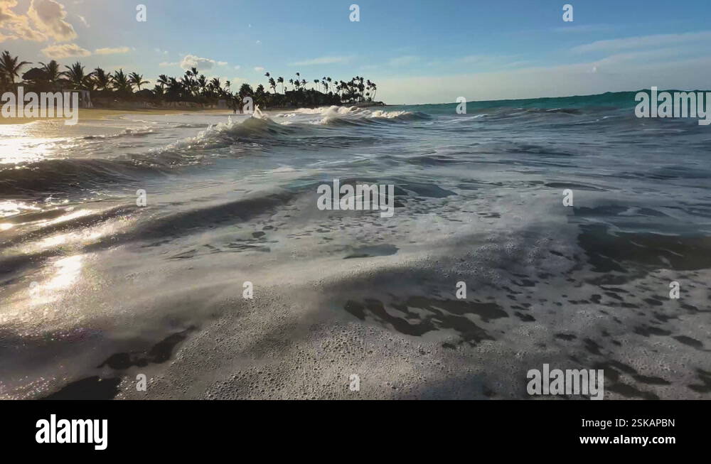 water level view of Caribbean waves crashing onto a sandy beach with a ...