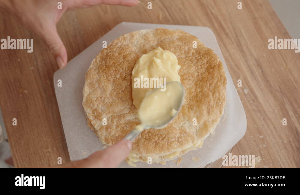 The pastry chef spoonfully spreads white cream onto the layers of puff ...