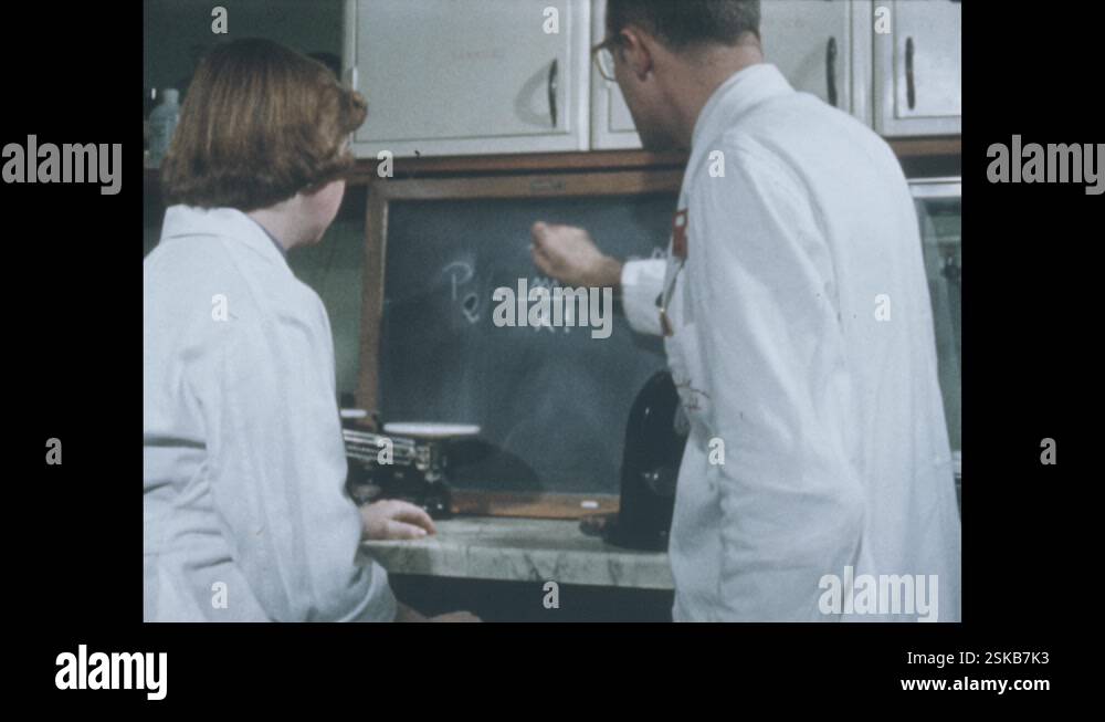 1960s: man and woman in lab coats talk, nod at marble lab table with ...