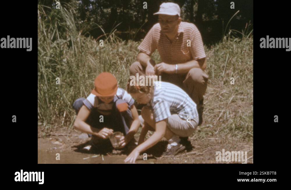 1960s: Man and kids kneeling by pond, kids pull tadpoles from water ...