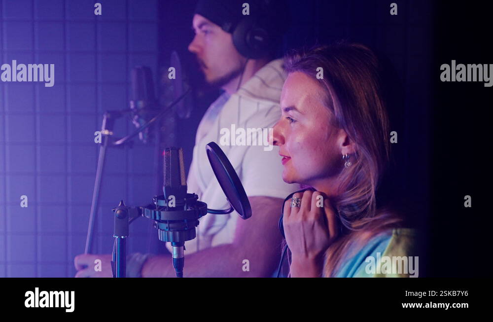 woman and man singers are singing to mic in isolation booth of modern ...