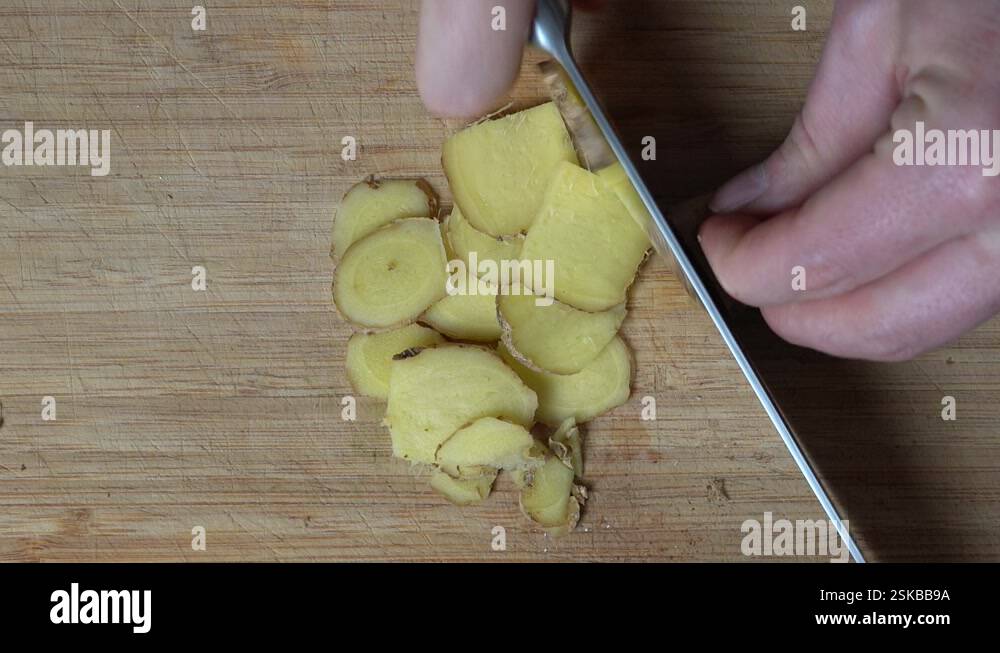 top down shot of fresh ginger being cut in slices on a kitchen board ...