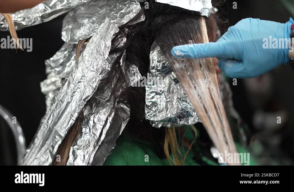 hairstylist in latex gloves using brush to smear dye on hair of woman ...