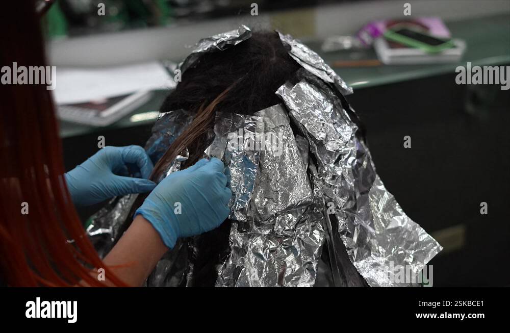 hairstylist in latex gloves using brush to smear dye on hair of woman ...