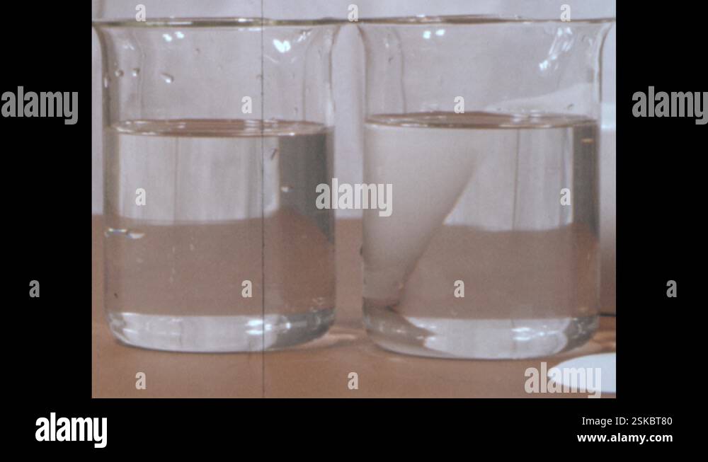 1960s: Two glass beakers of water. Scientist drops blue rock in one ...