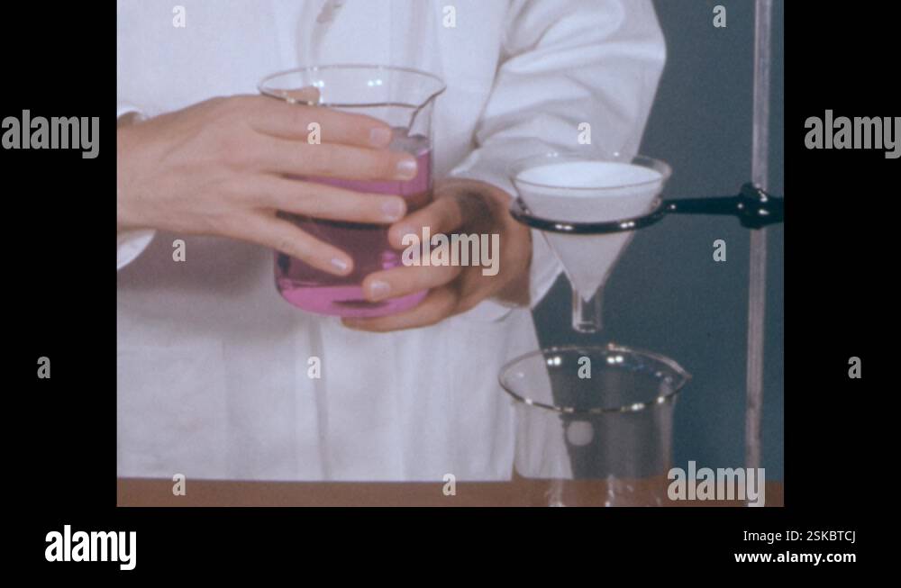 1960s: Scientist pours glass beaker of purple liquid through funnel ...
