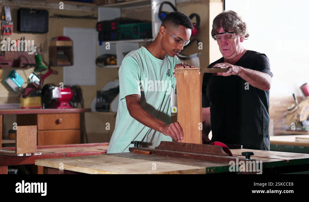 Candid senior carpenter guiding apprentice to use saw machine, slicing ...