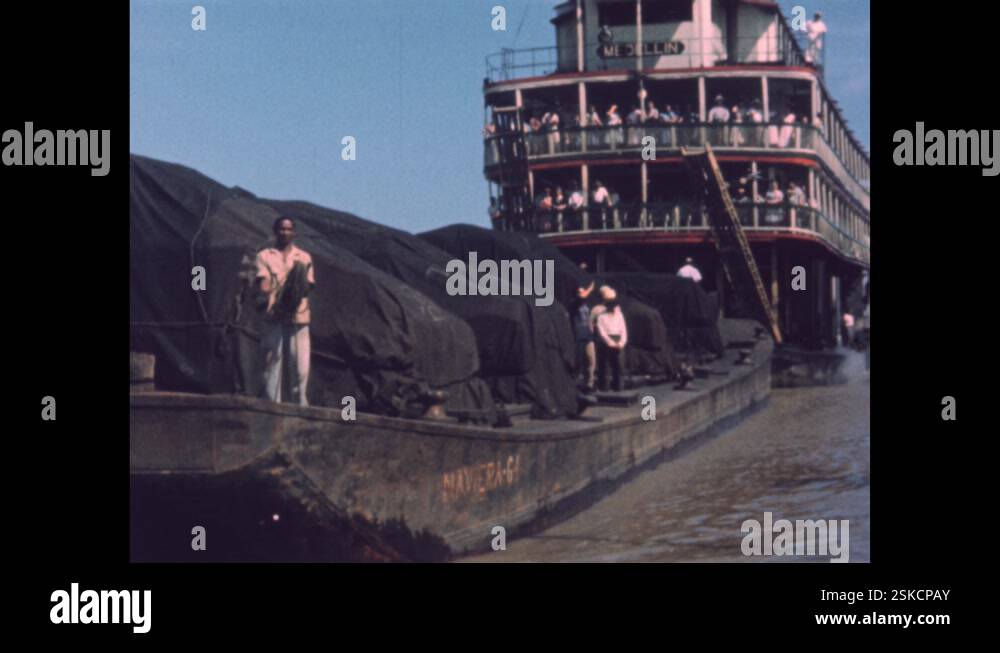 1960s: Men stand on a barge being pushed by a riverboat. Barge has ...