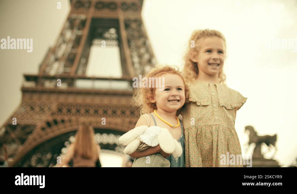 Two smiling little sisters hug each other and pose at the famous Eiffel ...