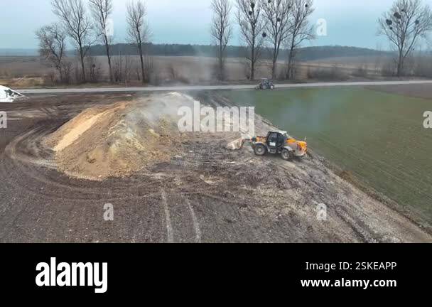 Agricultural loader spreading lime fertilizer across a large pile in an ...