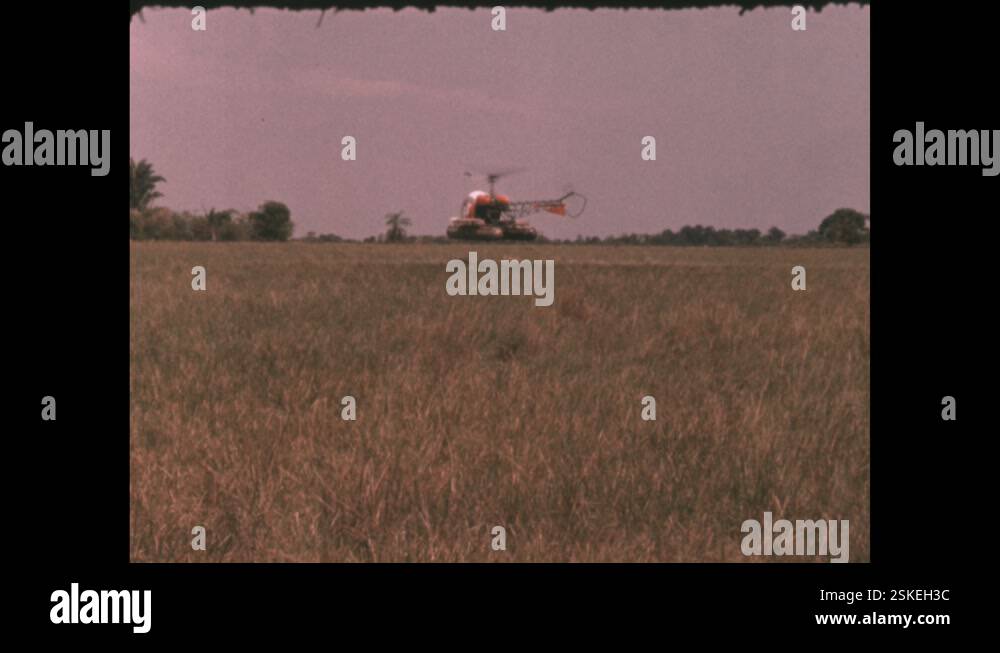 1960s: Helicopter flying over field, tilt down to wire unrolling from ...