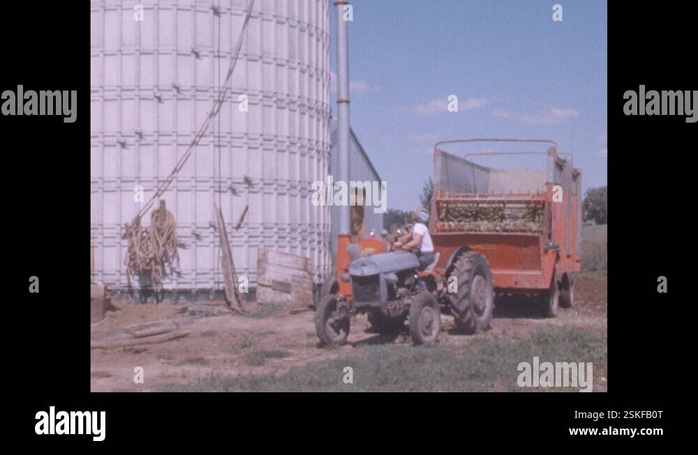 1960s: A farmer sits at a tractor while a hopper unloads silage into a ...
