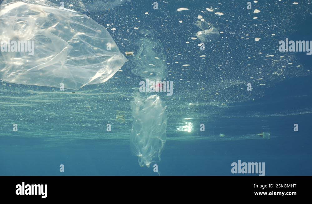 Plastic trash floating in blue sea of polluted water reflecting on its ...