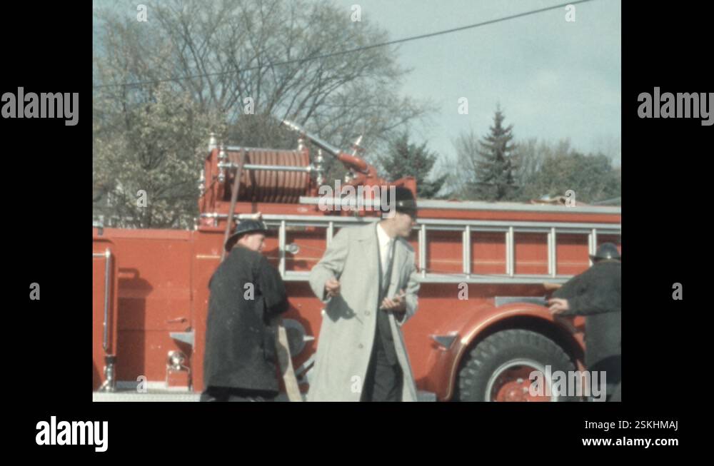 1960s: Firefighter rolls up hose. Reporter speaks to firefighter. Men ...