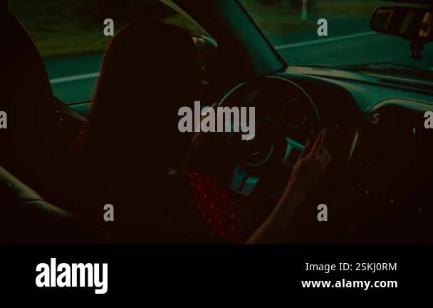 Woman driving car during evening, holding steering wheel, soft light ...
