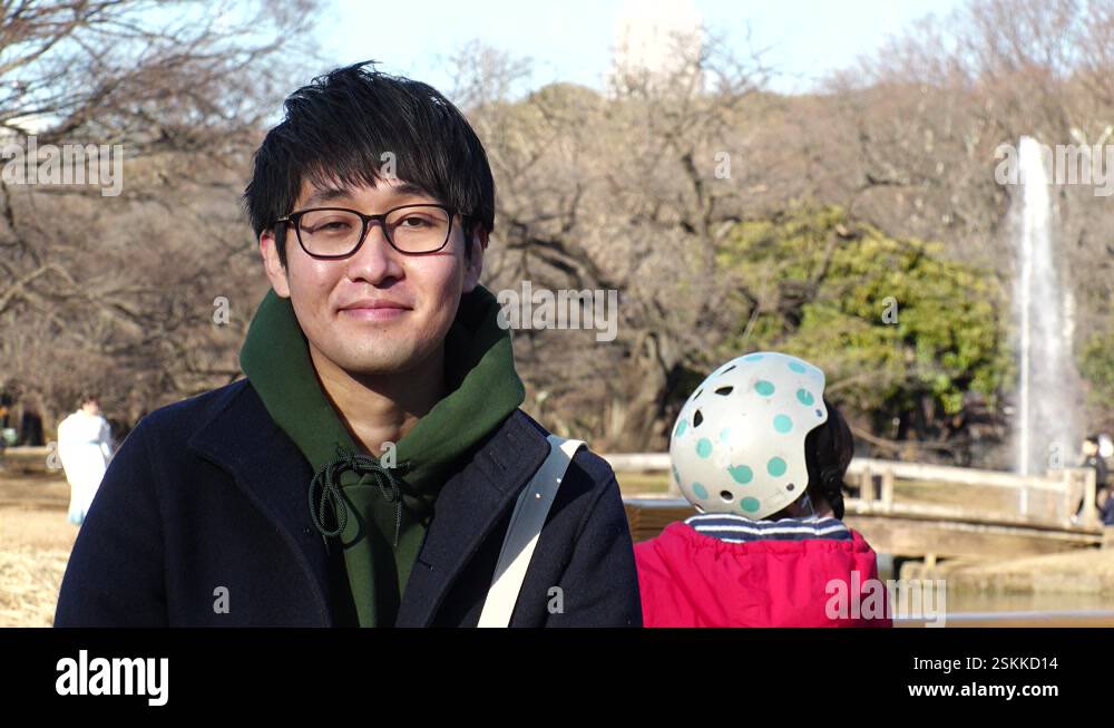 Asian (Japanese) young man sitting on the bench at the park in winter ...
