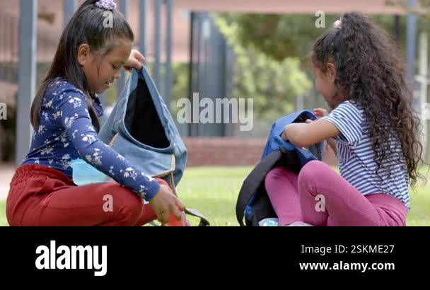 In school, two girls sitting on grass unpacking backpacks during break ...