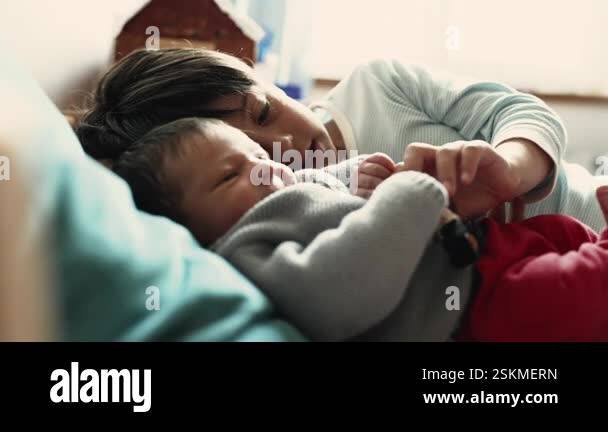 Older sibling and baby cuddle on a bed, sibling gently holding a toy in ...