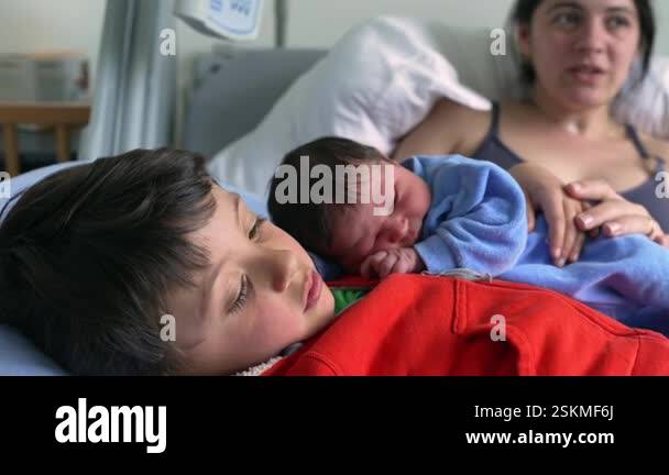 Big brother lying beside newborn baby in blue onesie on hospital bed ...