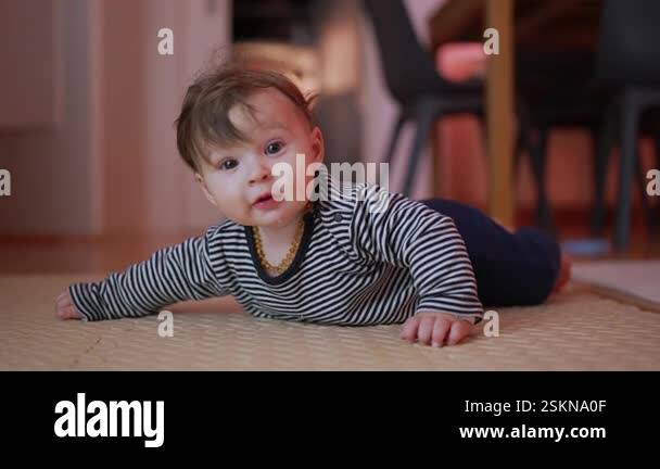 Baby lying on play mat, propped up on arms, curious expression ...