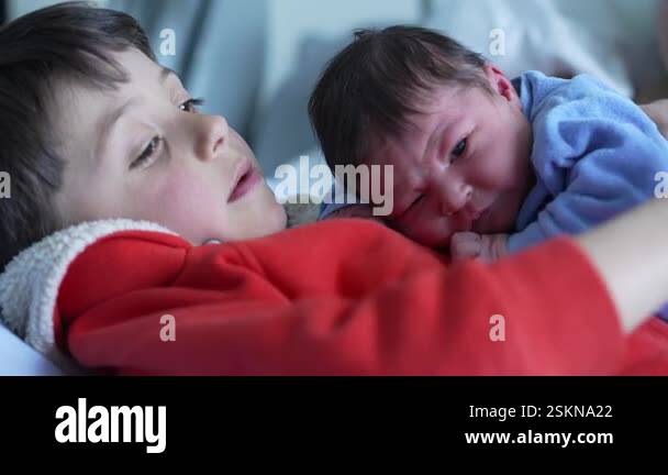 Older sibling lies back holding newborn baby close, capturing a ...