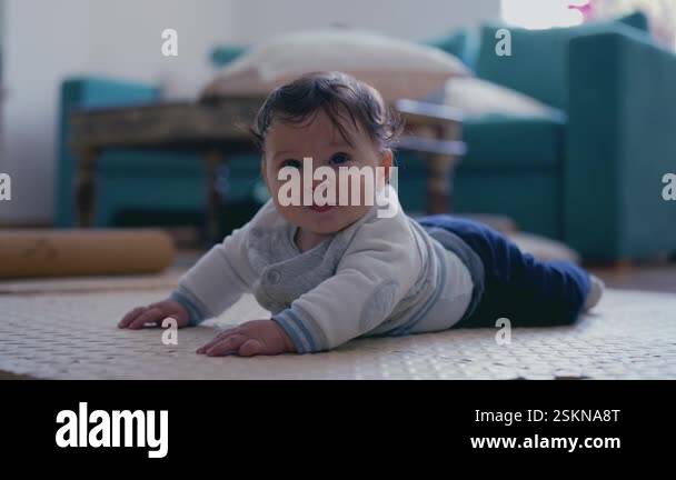 Baby lying on stomach on floor, smiling with curious expression ...