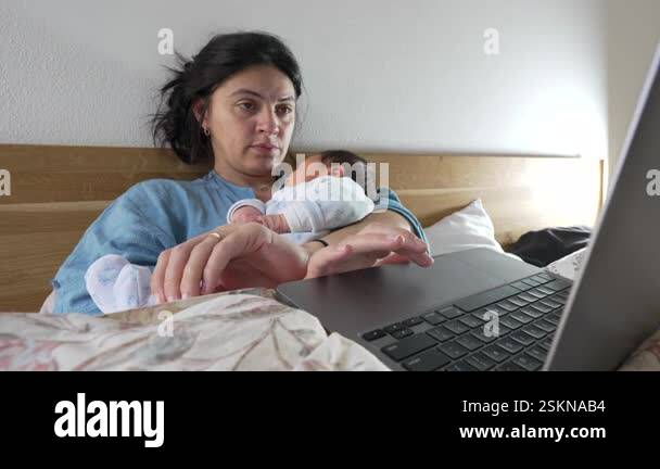Mother is focused on her laptop while her newborn baby sleeps in her ...