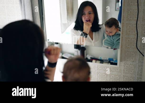 Mother brushing teeth holding baby, baby observing in bathroom, family ...