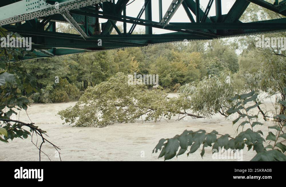 River floods overflows riverbed under bridge trees in water tilt up ...